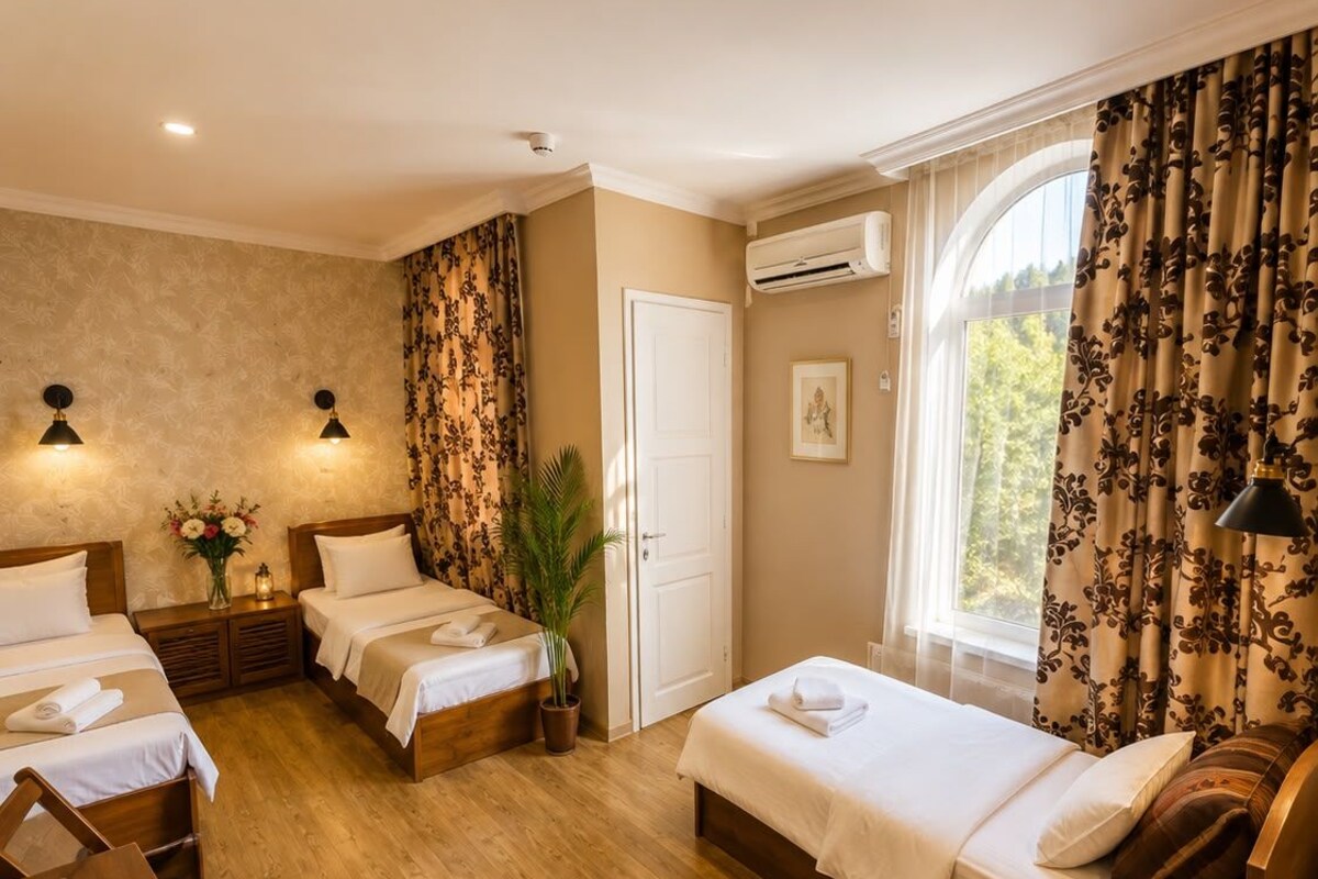 Quarto de hotel com duas camas de solteiro, um sofá-cama, uma mesa de jantar e uma janela grande com cortinas.