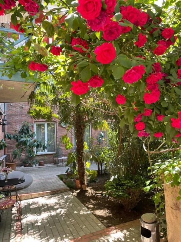 Um jardim com área de pátio, parede de tijolos e lixeira de metal.