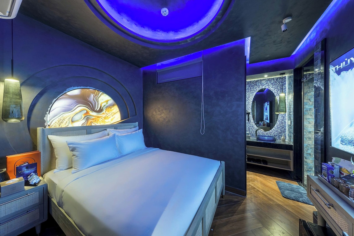 Quarto de hotel moderno com uma cama grande, uma toucador com espelho e uma televisão.