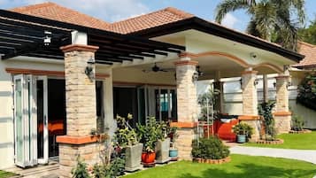 Uma casa moderna com um alpendre coberto, pilares de pedra e um gramado bem cuidado.
