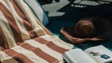 Uma cadeira de descanso com uma toalha listrada, um chapéu e um livro aberto.