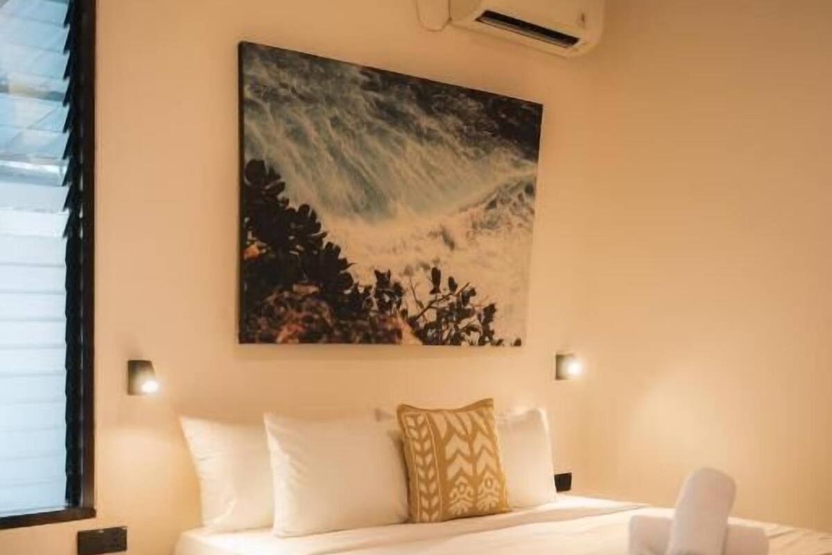 Quarto com cama, mesas de cabeceira, um quadro e um aparelho de ar condicionado.