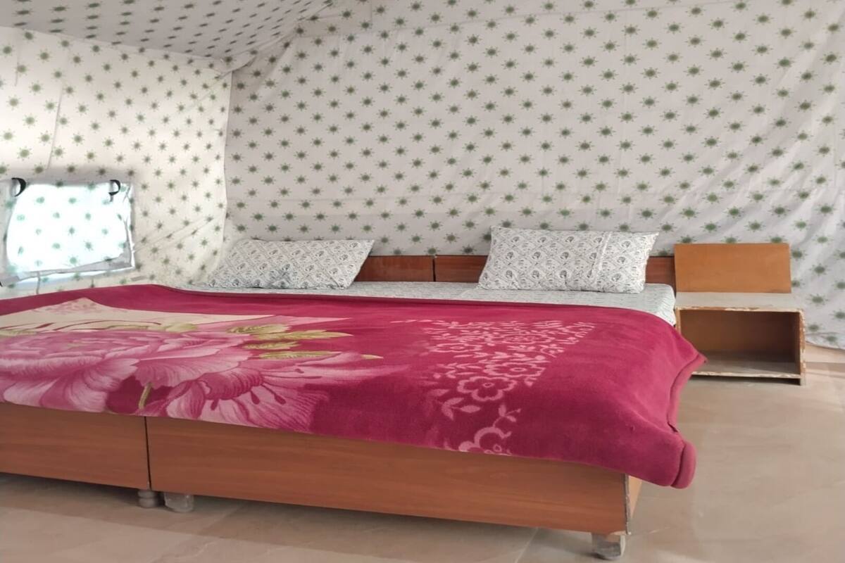 Um quarto com cama, almofadas, mesa de cabeceira e janela com cortinas.