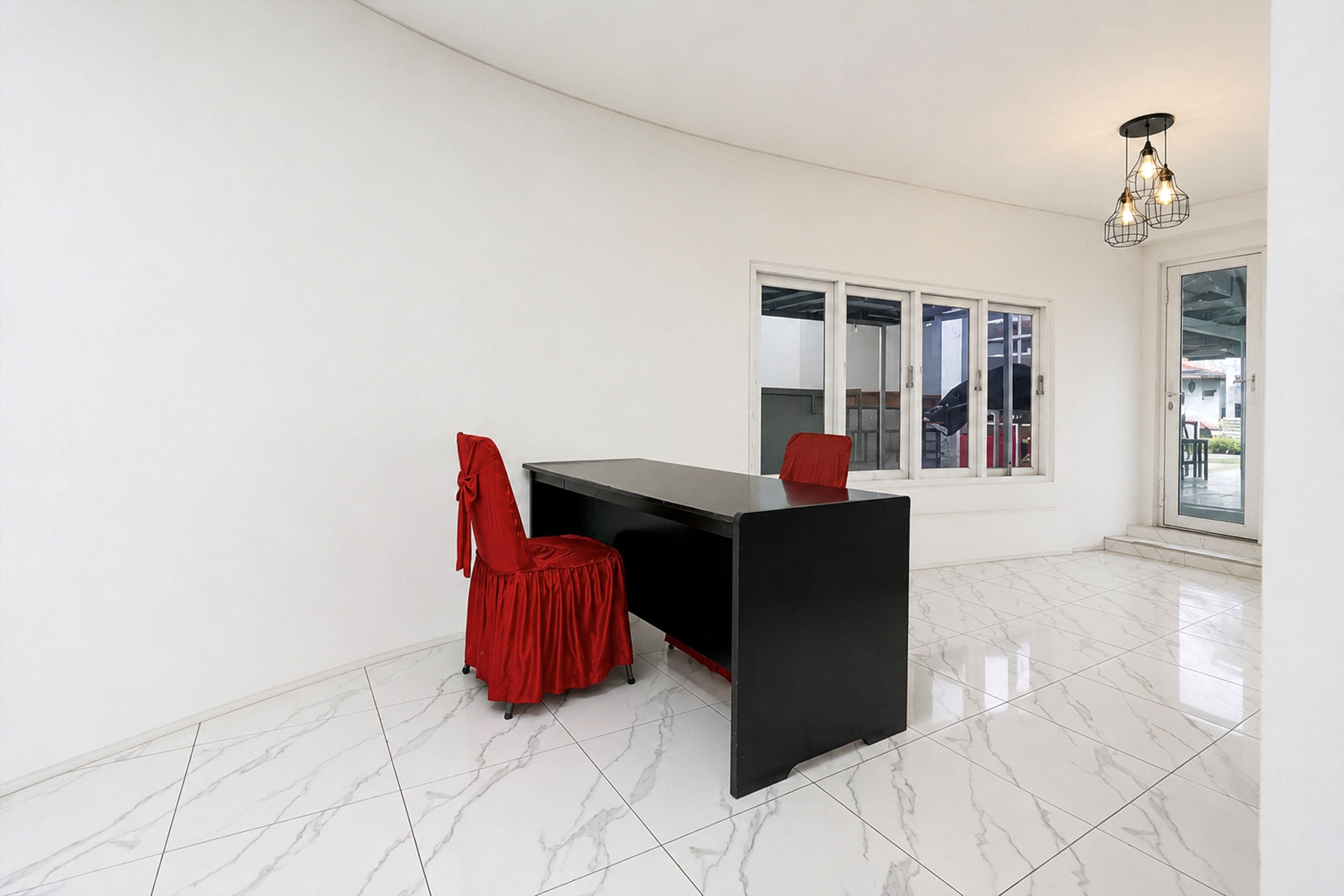 Quarto moderno com escrivaninha preta, duas cadeiras vermelhas, uma janela grande e um lustre.