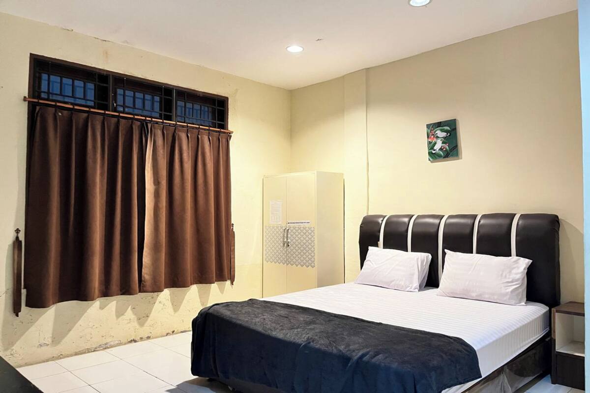 Quarto com cama, cortinas, guarda-roupa e uma pequena decoração na parede.