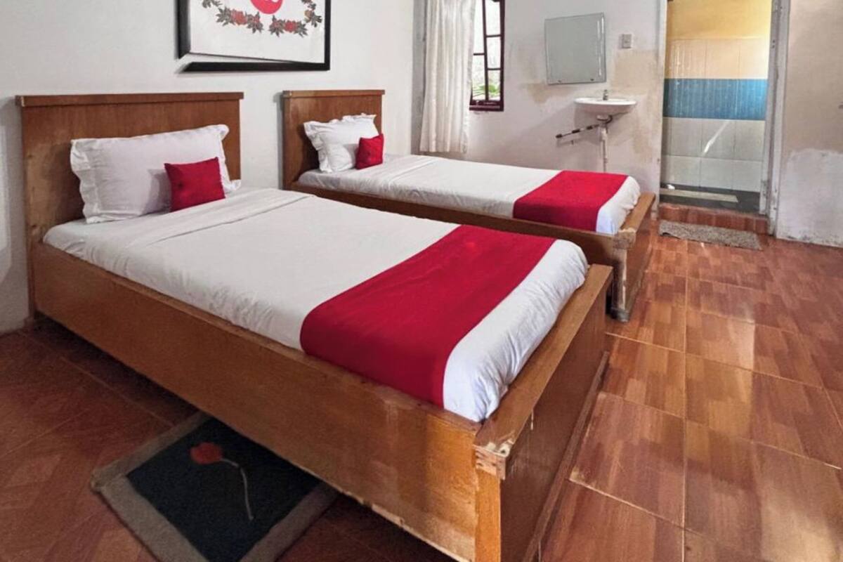 Duas camas de madeira com roupa de cama branca e vermelha, uma pia pequena e uma janela com cortinas.