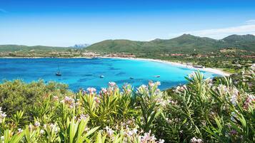 Paisagem costeira com águas azul-claras, barcos e uma praia.