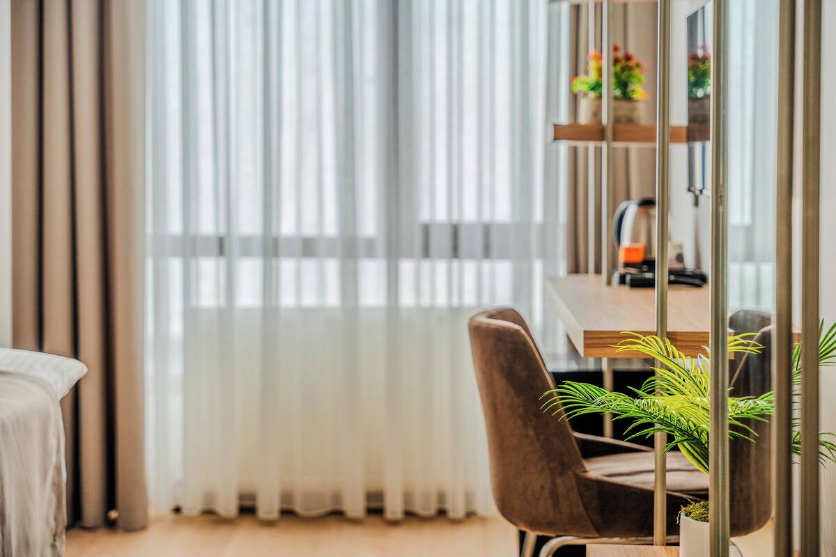 Um interior moderno com área de refeições, uma planta e uma janela com cortinas leves.