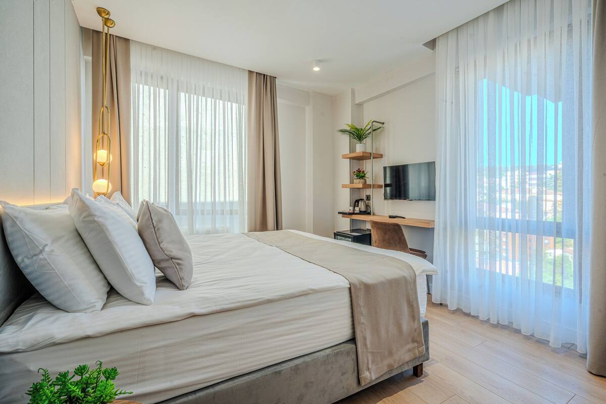 Quarto moderno com uma cama grande, televisão, planta e vista para a varanda.
