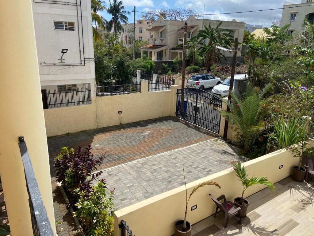 Zona residencial com um pátio pavimentado, plantas em vasos e portão fechado.
