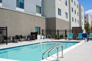 Piscina com escada de metal, rodeada por espreguiçadeiras e mesas, com um edifício de design moderno ao fundo.