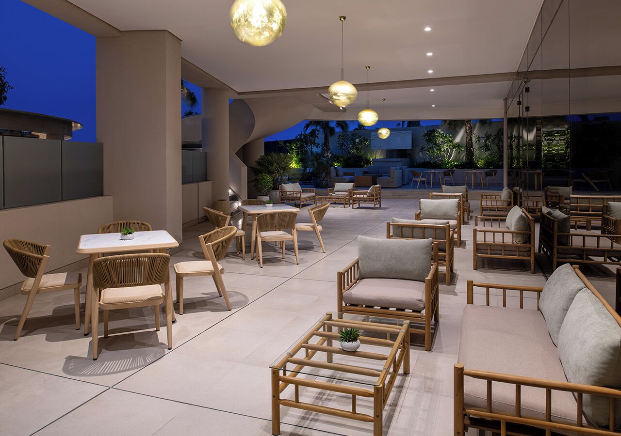 Uma área externa com mobiliário de vime, uma mesa de centro de vidro e iluminação pendente.