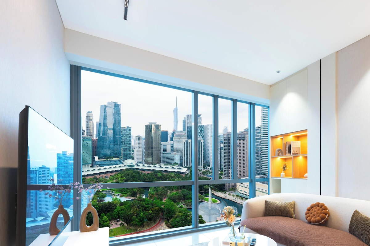 Uma sala de estar moderna com uma janela grande, um sofá, uma TV de tela plana e vista para a cidade.