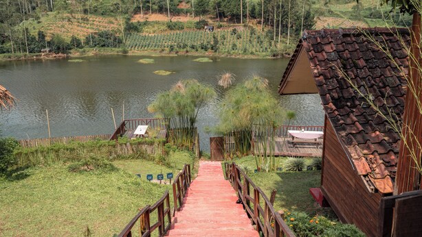 Uma escadaria de madeira leva a uma casa à beira de um lago, com um jardim cercado.
