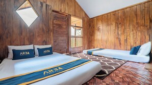 Quarto de hotel com paredes de madeira, uma cama com colcha da marca, um sofá e uma janela.