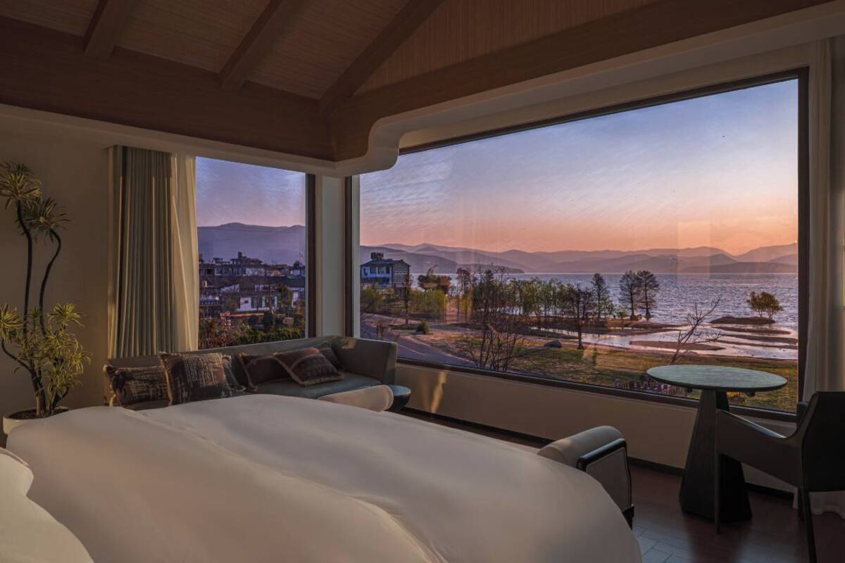 Quarto com uma cama grande, um sofá e vista para a paisagem costeira com montanhas.