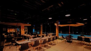 Uma área de refeições interna com mesas e cadeiras, uma piscina e um bar.