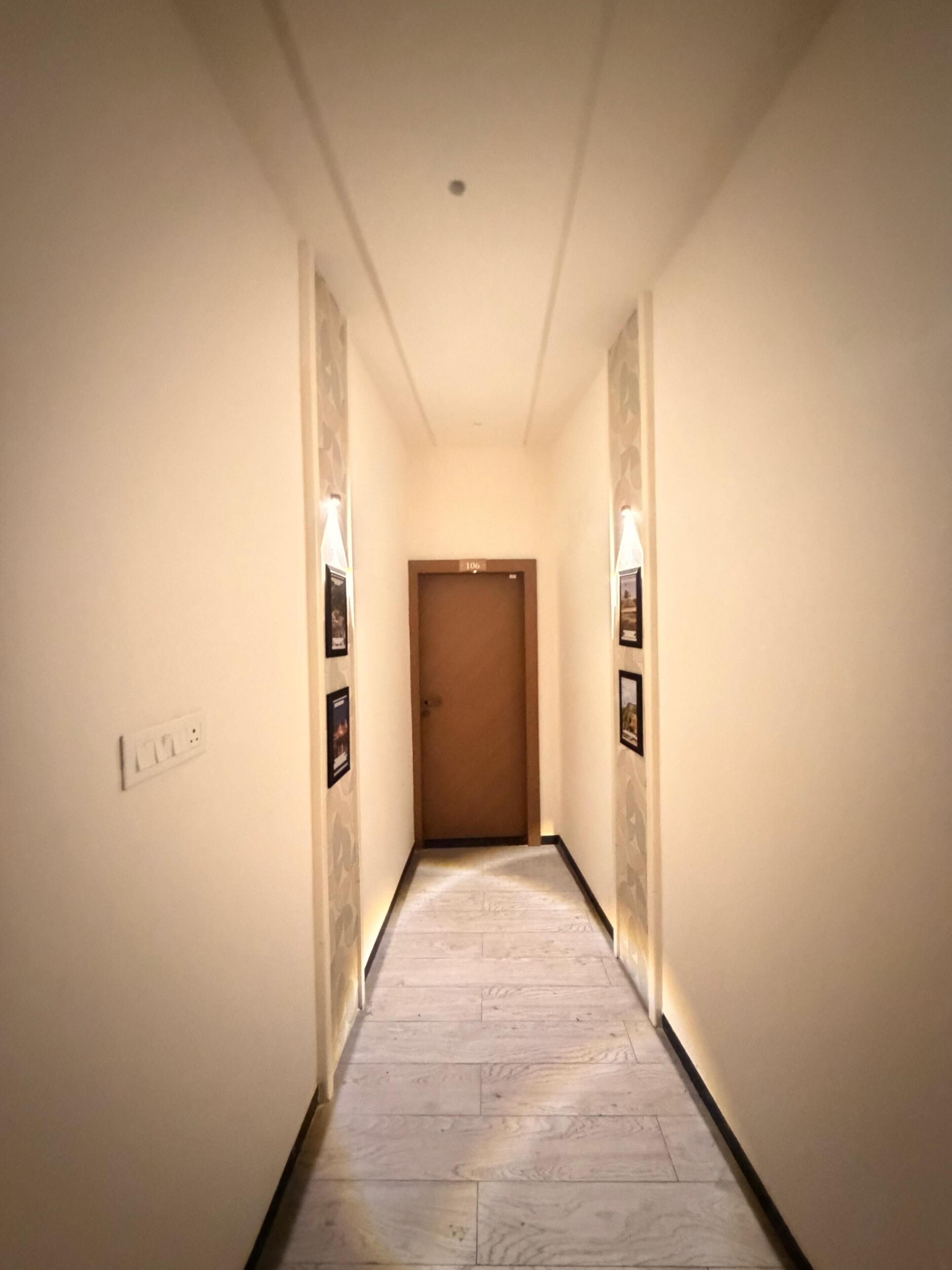 Um corredor estreito com uma porta no final, luminárias nas paredes e um interruptor de luz à esquerda.