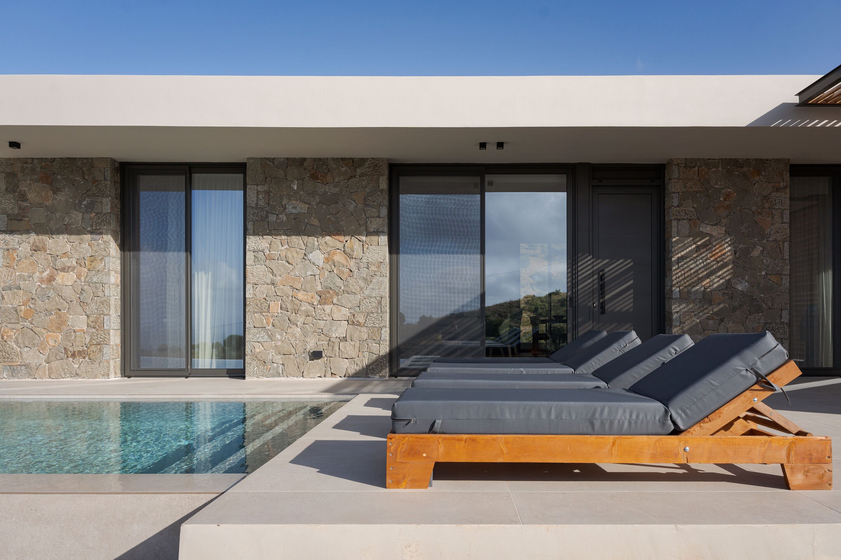 Um edifício moderno com fachada de pedra, piscina e espreguiçadeiras.