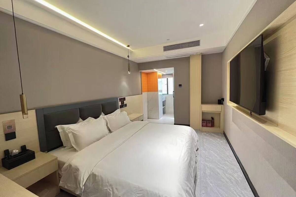Quarto de hotel moderno com uma cama grande, mesas de cabeceira, uma televisão e um banheiro visível por uma porta aberta.