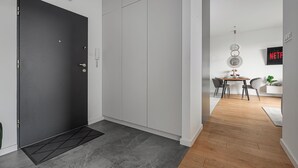Interior moderno com uma porta escura, armários cinzentos, piso de madeira e um espaço de refeições com cadeiras e mesa.