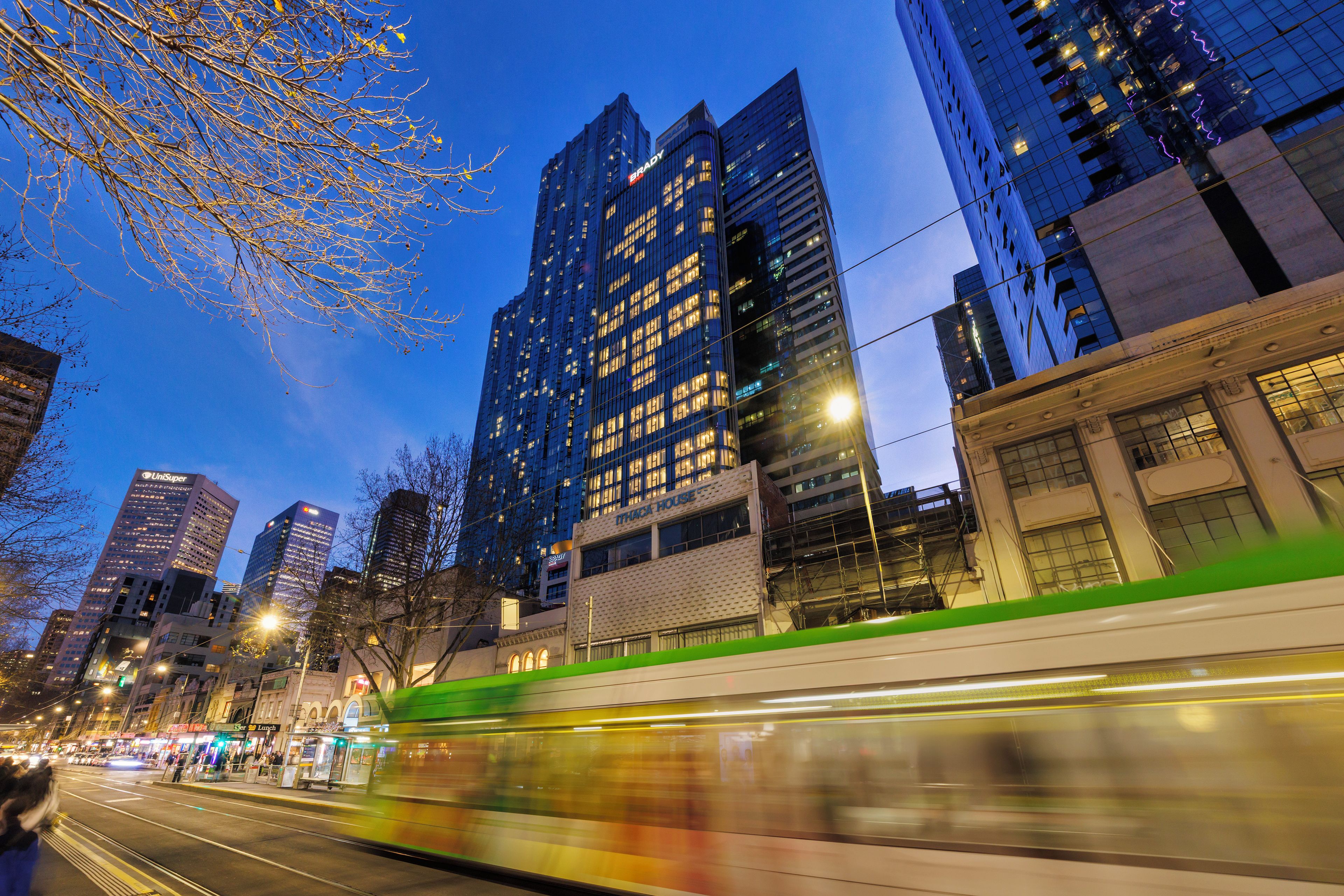 Paisagem urbana com edifícios altos modernos, um eléctrico em movimento e céu claro.