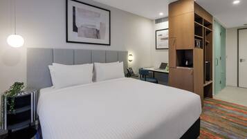 Quarto de hotel com cama, mesa de cabeceira, abajur, obra de arte emoldurada e armário embutido.