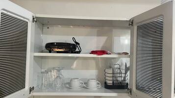 Um armário de cozinha com um micro-ondas, uma faca de cabo vermelho e um porta-utensílios.