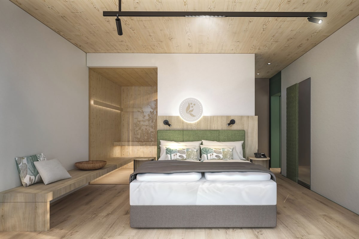 Quarto moderno com teto de madeira, cama com roupa de cama branca, mesa de cabeceira e luminária fixada na parede.