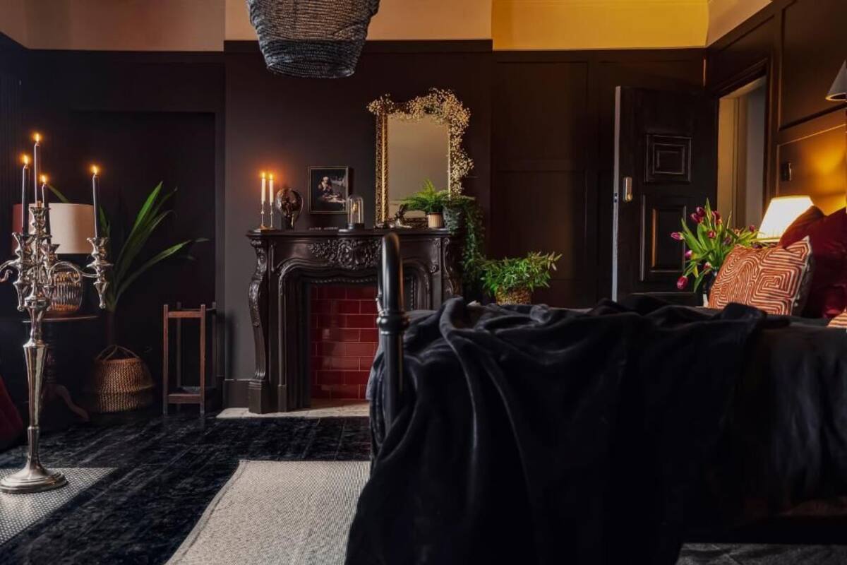 Quarto em tons escuros com lareira, candelabro e cama com cobertura preta.