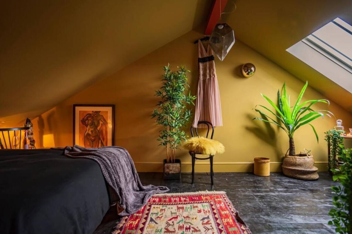 Um quarto aconchegante com uma cama, uma cadeira, uma mesinha, uma planta em vaso e um quadro na parede.