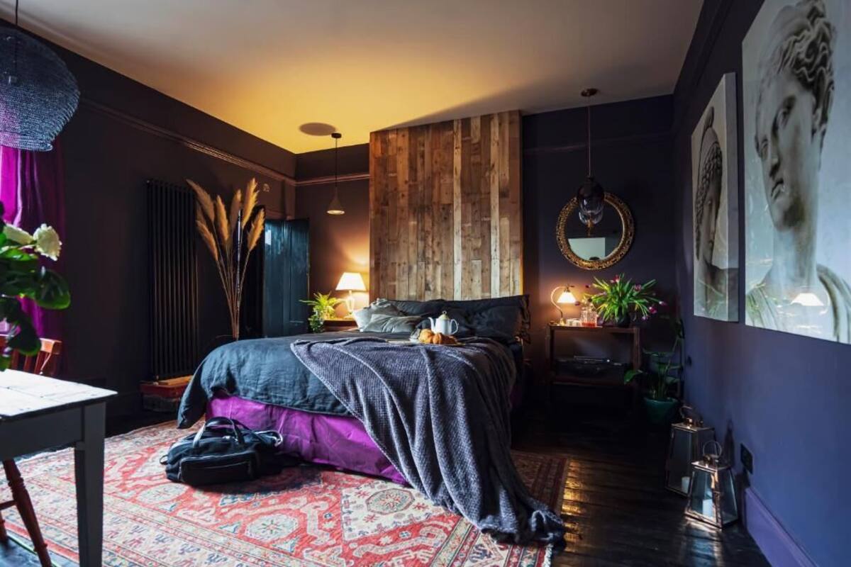 Um quarto com cama, mesas de cabeceira, luminárias, um espelho e uma janela grande.