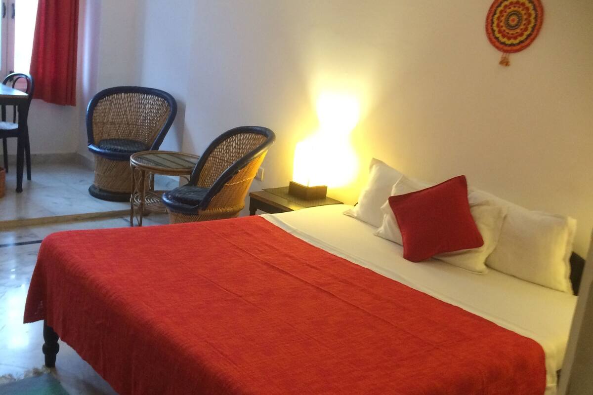 Um quarto com uma cama, uma cadeira, uma mesa e um objeto decorativo na parede.