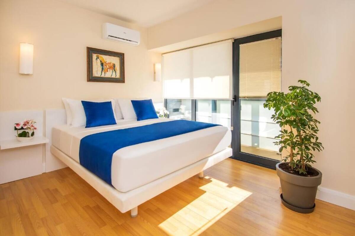 Quarto com cama, planta em vaso, janela com persianas e ar condicionado fixado na parede.