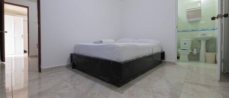 Quarto com cama, banheiro com pia e vaso sanitário, e porta que dá para outro cômodo.