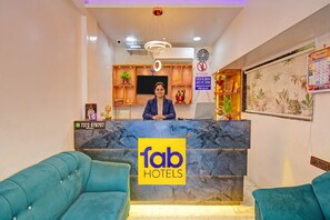 Balcão de recepção de hotel com logotipo 'fab hotels', um relógio, um calendário e um aviso de proibição de bebidas.