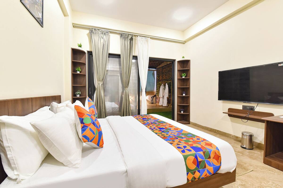 Quarto de hotel com cama, televisão, guarda-roupa e uma pequena planta.