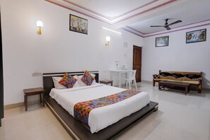 Quarto de hotel com cama, escrivaninha, cadeira, sofá e ventilador de teto.