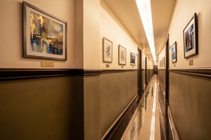 Um corredor com obras de arte emolduradas nas paredes, piso polido e luminária no teto.