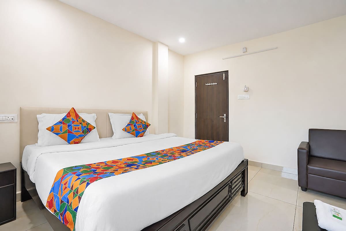 Quarto de hotel com cama, cadeira, porta e tomadas.