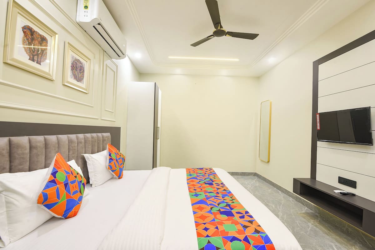 Quarto de hotel com cama, almofadas, televisão, ar condicionado e ventoinha no teto.