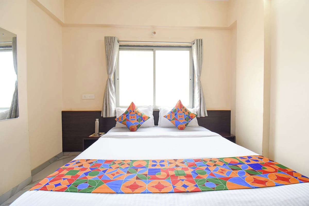 Quarto de hotel com uma cama, uma janela com cortinas e um edredom colorido.