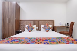 Quarto de hotel com cama, duas almofadas, uma cadeira, mesa de cabeceira, mesa e armário.