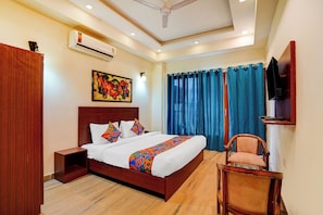 Quarto de hotel com cama de madeira, mesa de cabeceira, televisão na parede e ventoinha de teto.