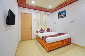 Quarto com cama de madeira, cortinas brancas, um quadro na parede e televisão montada.