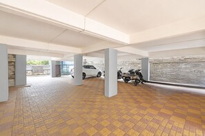 Uma área de estacionamento coberta com piso quadriculado, pilares brancos e uma parede de pedra.