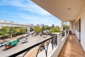 Uma varanda com vista para uma rua movimentada, uma passarela para pedestres e um edifício com o letreiro 'GMEZA'.