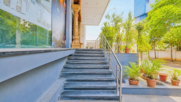 Escadaria que leva a um edifício com fachada de vidro e plantas em vasos.