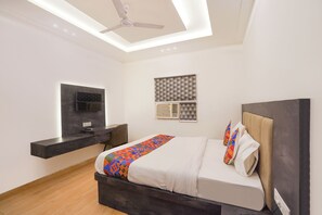 Um quarto com uma cama, escrivaninha, ventilador de teto, televisão e ar condicionado.