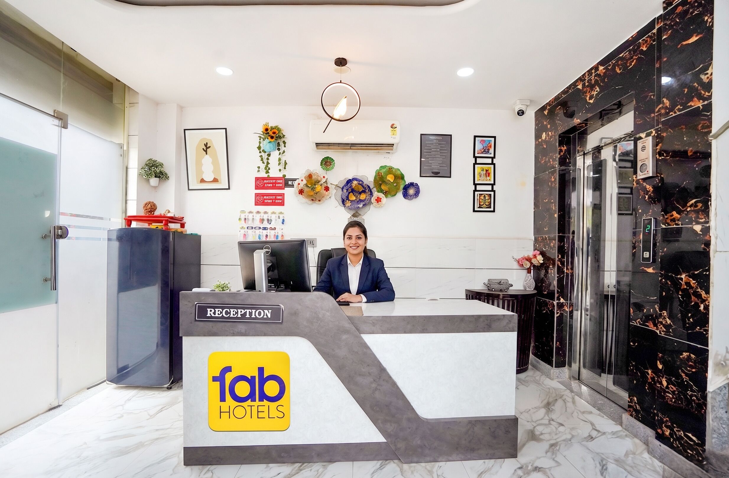 Uma receção com o logótipo 'fab hotels', um rececionista e um interior moderno com pavimento em mármore e arte decorativa nas paredes.